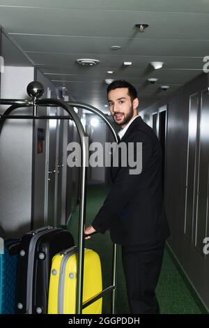 Cheerful smiling professional bellboy in formal attire with baggage ...