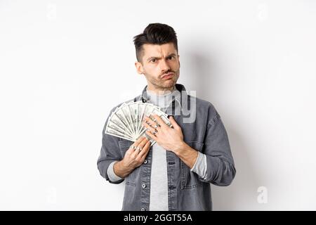 Greedy guy frowning and hugging dollar bills, unwilling to share money ...