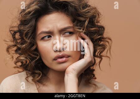 Young curly hispanic woman frowning and looking aside isolated over ...