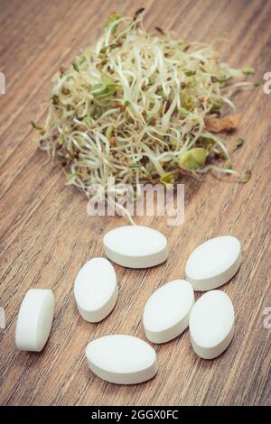 Alfalfa and radish sprouts with tablets supplements on wooden surface ...