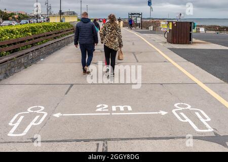 People walk past a Social Distancing sign in Oxford Circus on a clear ...