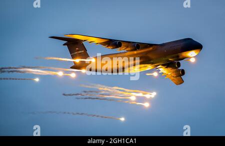 A 436th Airlift Wing C-5M Super Galaxy crosses an orange sky at sunset ...