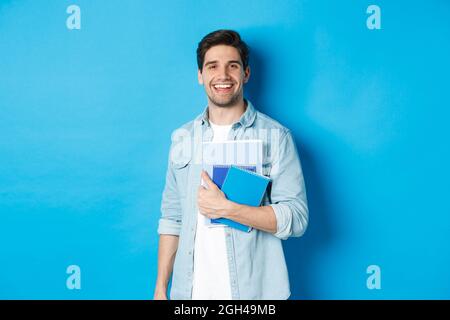 Smiling man studying, holding notebooks and looking happy, standing ...
