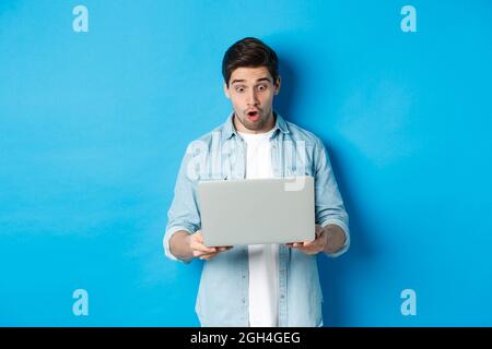Impressed caucasian guy looking at laptop screen with amazement ...
