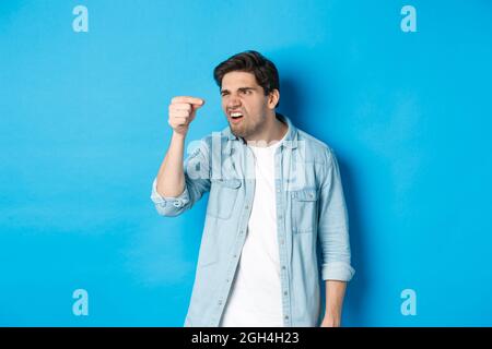 Confused guy holding something tiny in fingers and looking at it ...