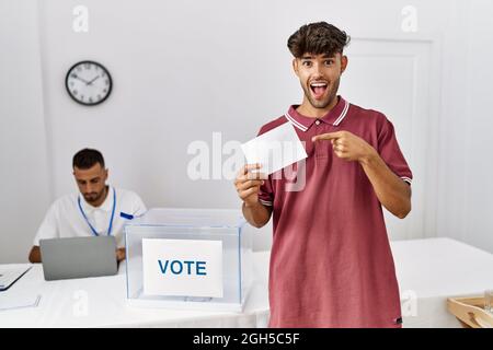 Young hispanic man voting putting envelop in ballot box smiling ...
