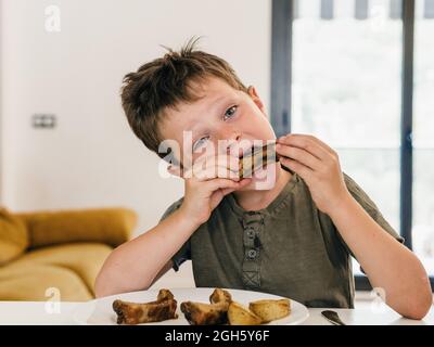 Adorable kid eating appetizing pork ribs during lunch at home and ...