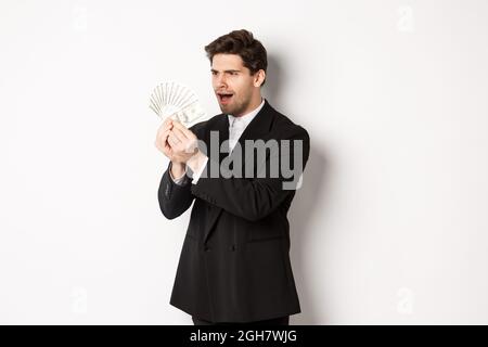 Image of confused businessman looking at fake money, standing over ...