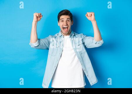 Happy attractive man triumphing, screaming yes and raising hands up to ...