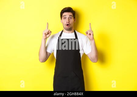 Surprised male waiter in black apron showing logo or advertisement ...