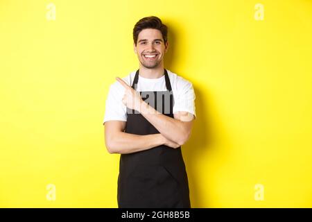 Happy barista pointing finger left and smiling, wearing black apron ...