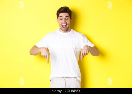 Image of amused handsome guy in white t-shirt, looking and pointing ...