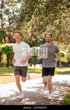 Cheerful smiling friends in sportswear running in the city dicussing ...