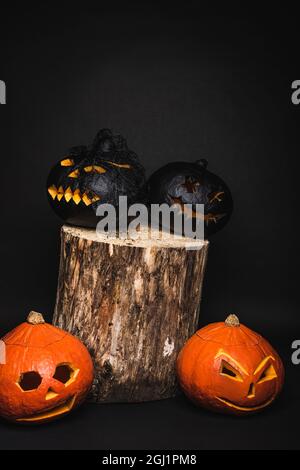 creepy and carved pumpkins on wooden stump near burning candle on black ...