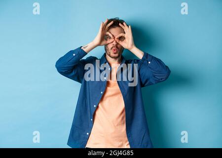 funny young man looking through binocular with huge smile on his face ...