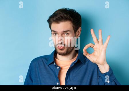 Image of silly young man pucker lips and show okay gesture, praise good ...