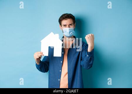 Real estate and covid concept. Cheerful guy in medical mask showing ...
