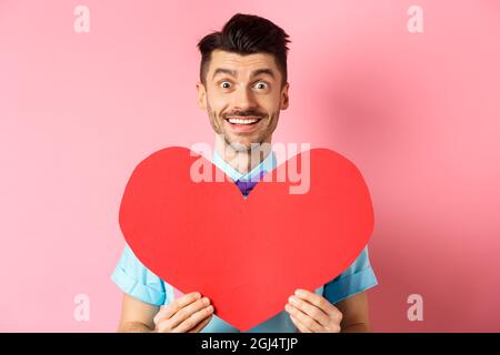 Hopeful man in love showing red heart sign, smiling at camera, waiting ...