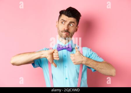 Confused guy looking pensive while judging, showing thumbs up and down ...