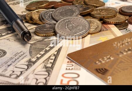 credit card and ink pen lying on a background of banknotes and coins of ...