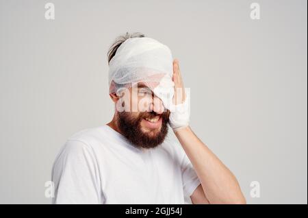 bearded man with bandaged head and eye hospitalization light background ...