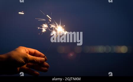 Hand holding a sparkler on beach during sunset with bokeh light ...