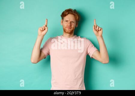Skeptical and disappointed redhead man pointing fingers up, frowning ...