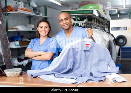Two workers offering professional dry cleaning, showing clean clothing ...