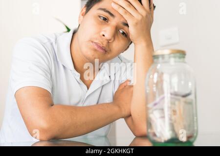 young guy crestfallen looking at his savings in a glass jar. young man ...