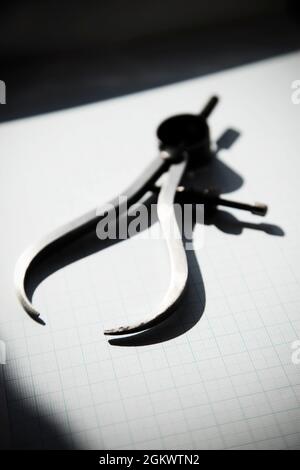 Metal outside spring calipers casting abstract shadow on piece of graph ...