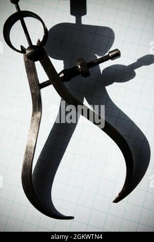 Metal outside spring calipers casting abstract shadow on piece of graph ...
