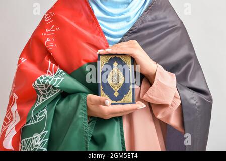 Woman with flag of Afghanistan and Koran on light background, closeup ...