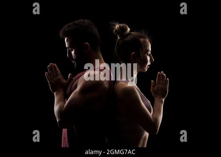 Fit couple posing together. Boy and girl praying back to back side lit ...