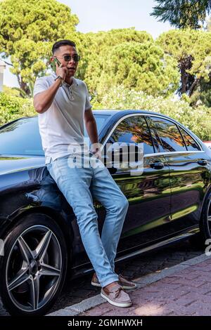 Busy young man stands and talks on phone holds box with ribbons and ...