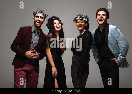 laughing multiethnic friends in halloween costumes looking at camera ...