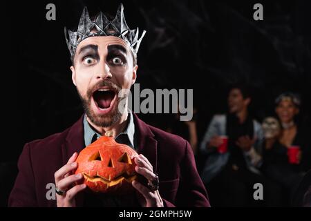 amazed man in vampire king halloween crown looking at camera on black ...