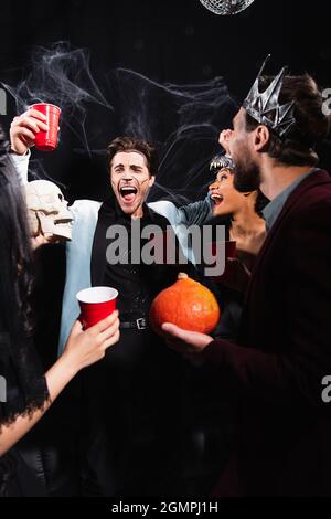 laughing multiethnic friends in halloween costumes looking at camera ...