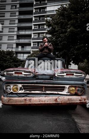Hispanic man with a thoughtful face smoking and posing with an old vintage car on a street Stock ...
