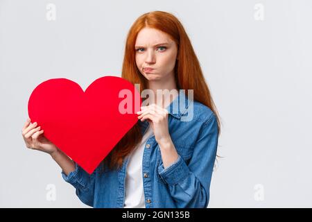 Serious-looking troubled, unsure cute redhead girl thinking what gift ...