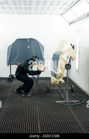 Auto painter in a protective suit and mask sprays a thinner or other ...
