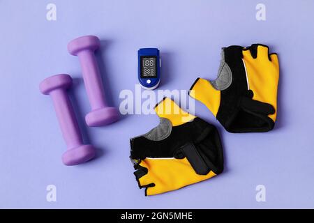 Pulse oximeter, dumbbells and bicycle gloves on color background Stock Photo - Alamy