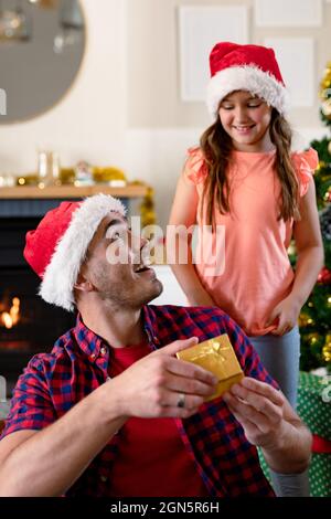 Surprised caucasian father wearing santa hat receiving present from his ...
