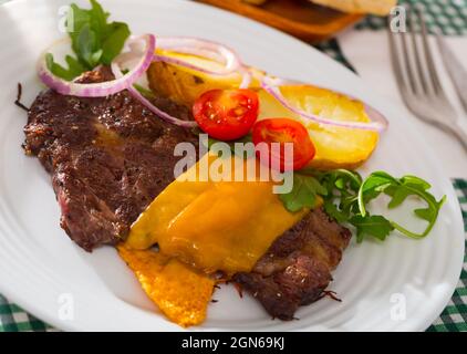 Well-done beef steak with cheese and baked potatoes at plate Stock ...