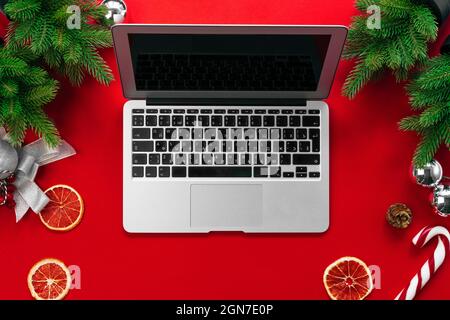 Laptop with fur tree branches and christmas decorations on red ...