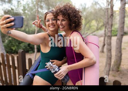 Happy woman photographing friend through smart phone by wall Stock ...