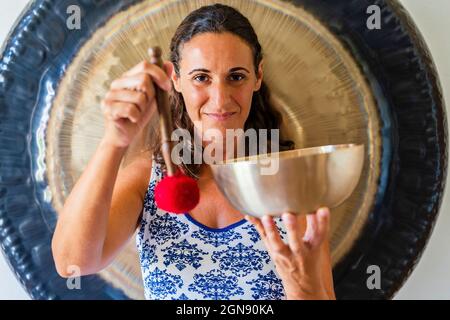 Portrait of smiling mature woman singing in kitchen with wooden spatula ...