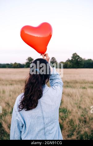 Young woman with heart-shaped balloon and bag on red background ...