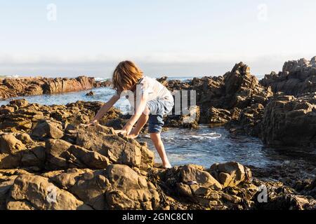 A young boy exploring the rock pools on a jagged rocky Atlantic Ocean ...
