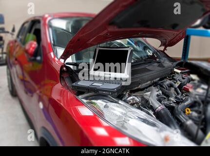 Car in a workshop and a computer running diagnostics on the engine ...