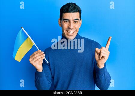 Handsome hispanic man wearing ukraine flag smiling happy pointing with ...